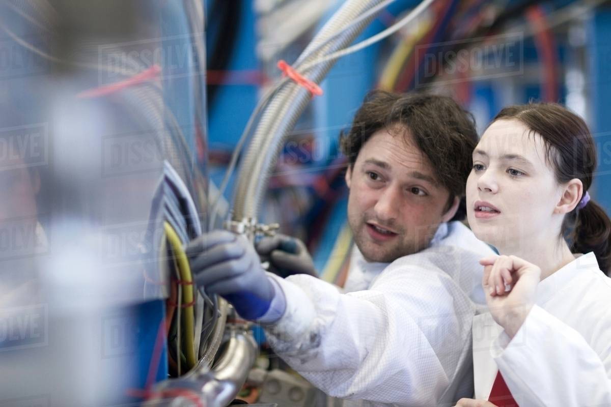 Male and female colleagues wearing lab coats inspecting wires - Stock ...