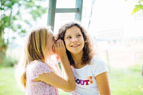 Two tween girls in garden whispering - Stock Photo - Dissolve