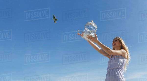 Young woman releasing bird from cage toward blue sky - Stock Photo ...