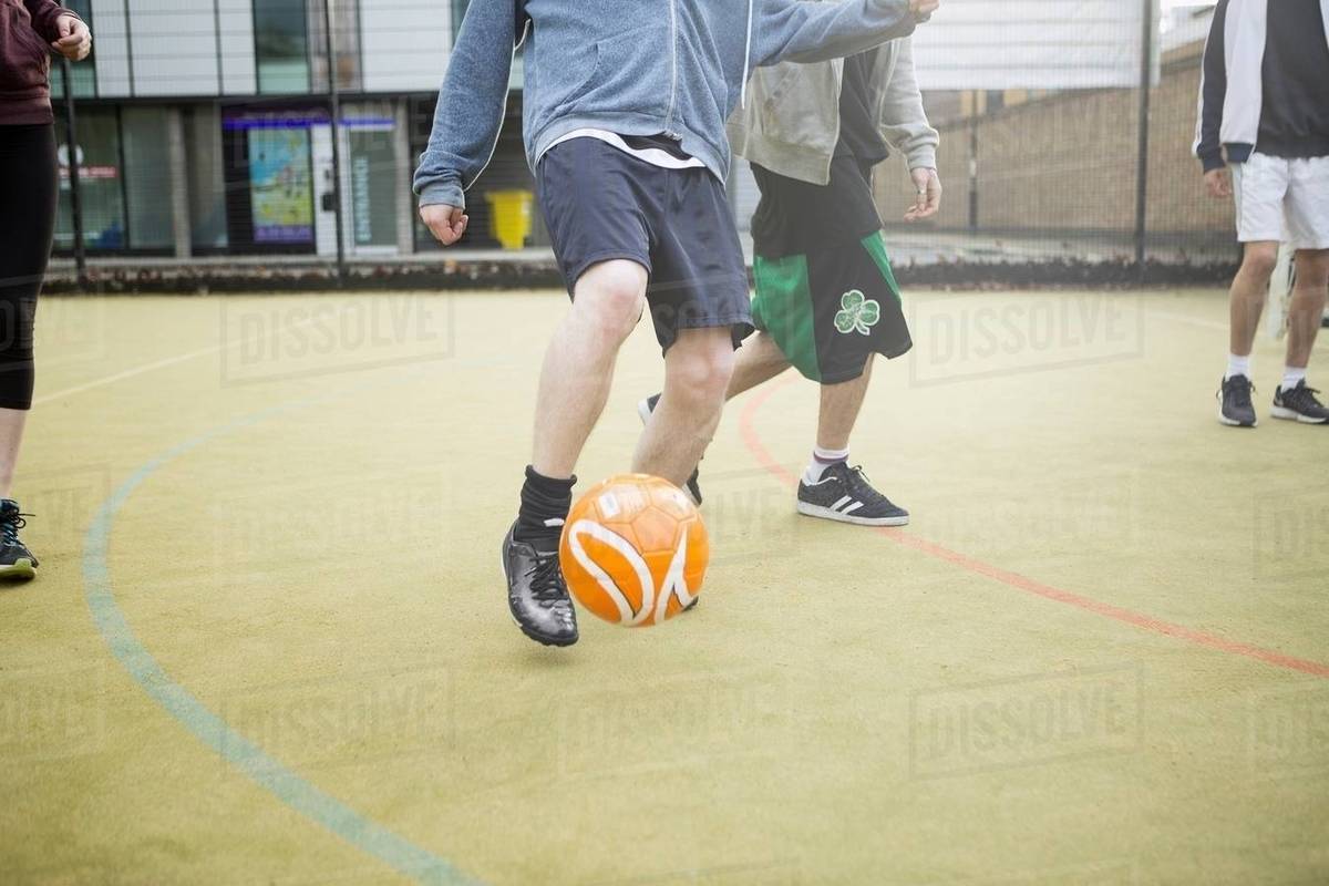Group of adults playing football on urban football pitch, low section ...
