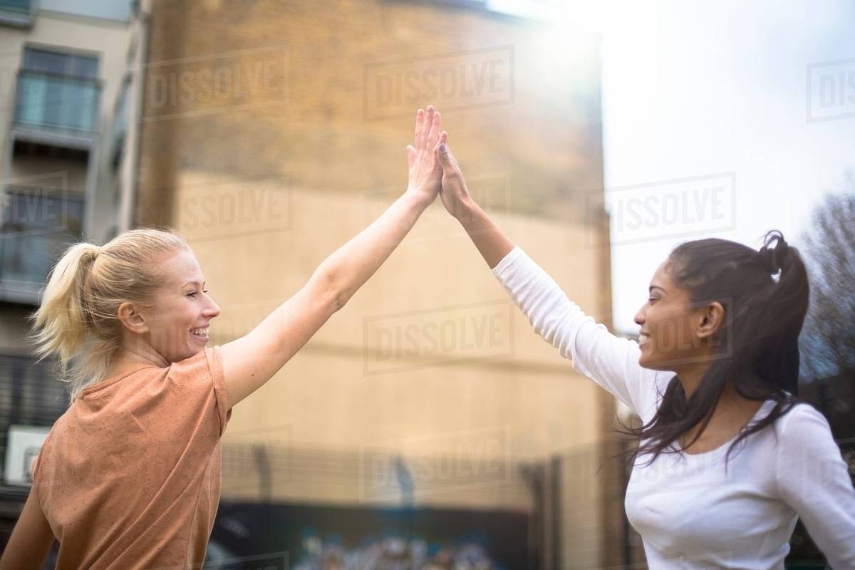Two young women giving high five, outdoors - Stock Photo - Dissolve