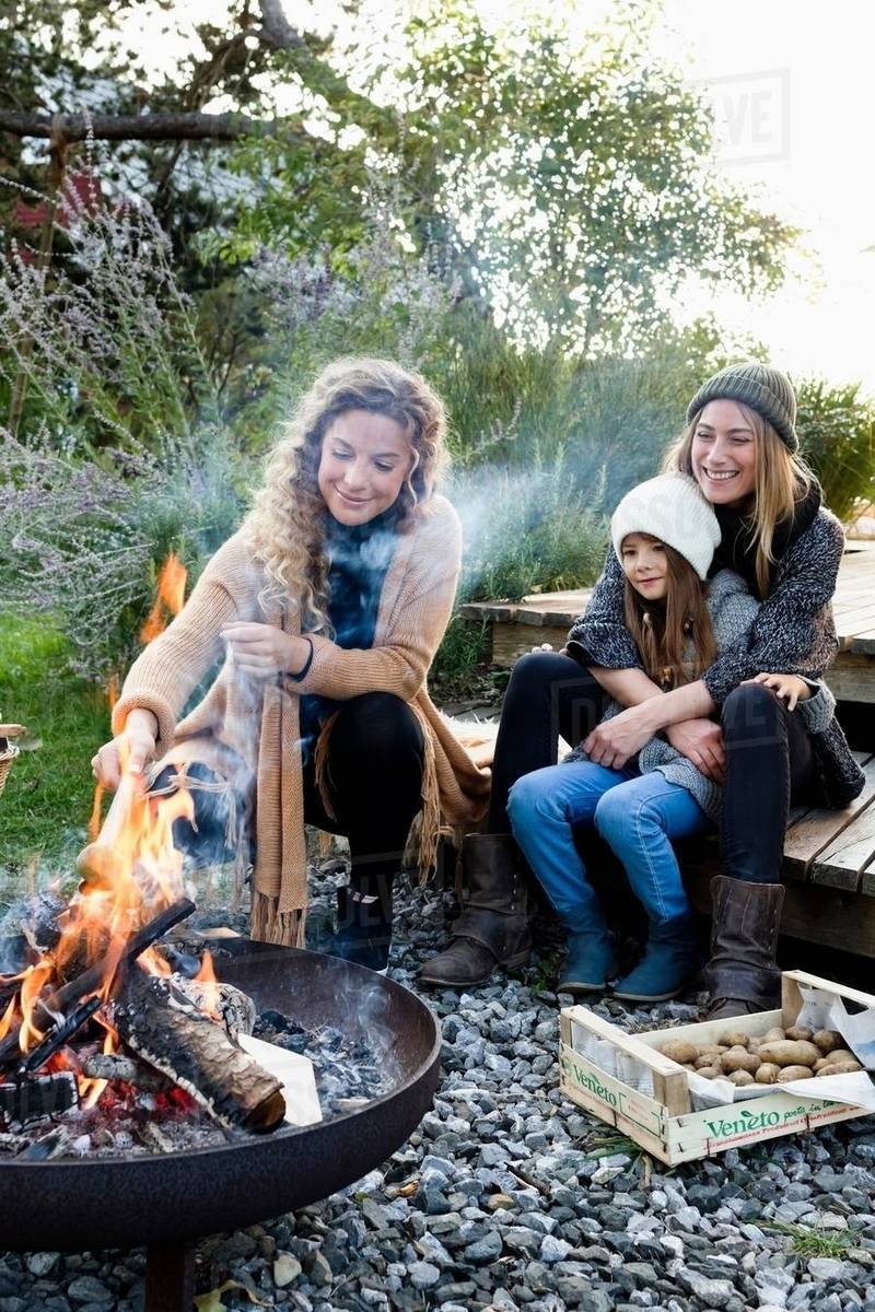 Two women and girl sitting by fire pit, relaxing - Royalty-free Stock ...