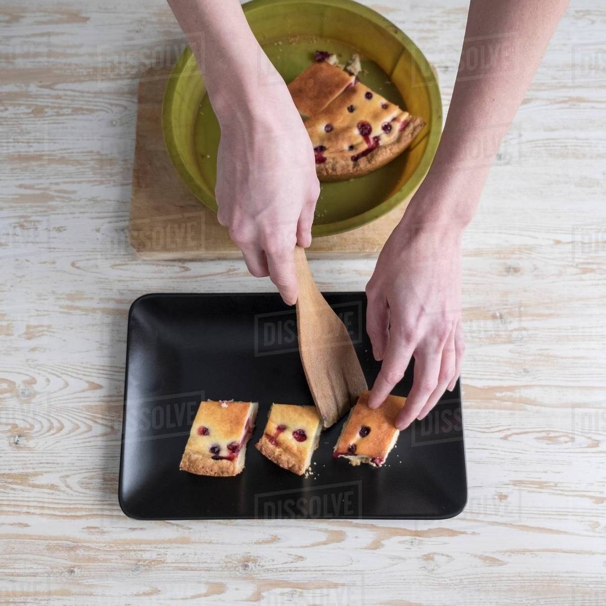 Overhead view of female hands placing cake onto dish at kitchen counter ...