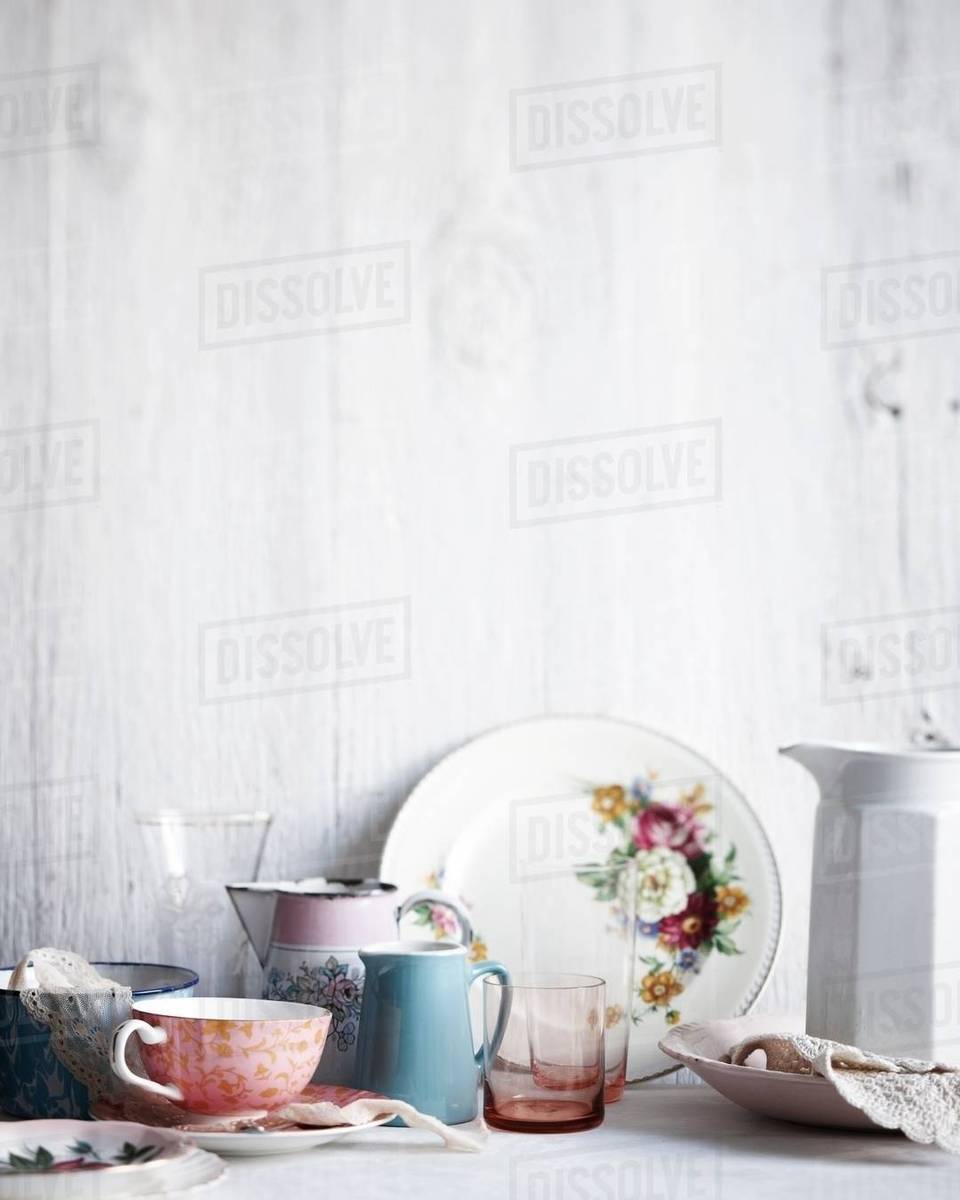 Variety of drinking glasses, plates and jugs on whitewashed table ...