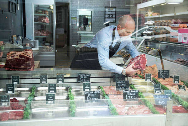 Butcher preparing window display in butcher's shop - Stock Photo - Dissolve