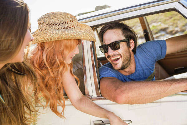 Two women flirting with man at car window on coast road, Cape Town ...