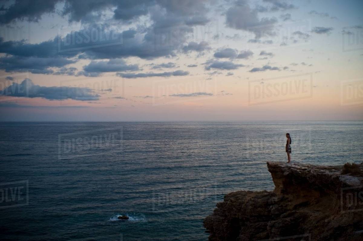 Woman standing on cliff looking out to sea at sunset - Stock Photo ...