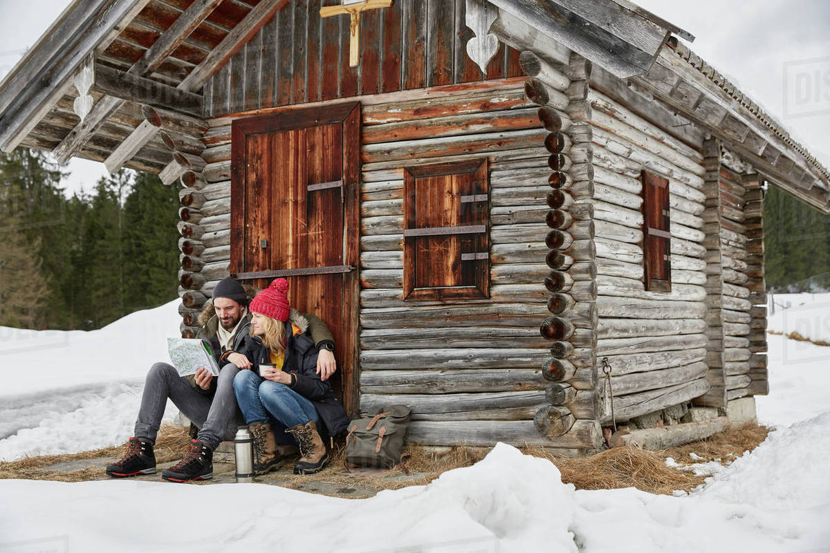 Couple reading map sitting outside log cabin in winter, Elmau, Bavaria ...