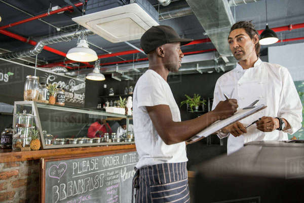 Employee in restaurant talking with chef, making notes on clipboard ...