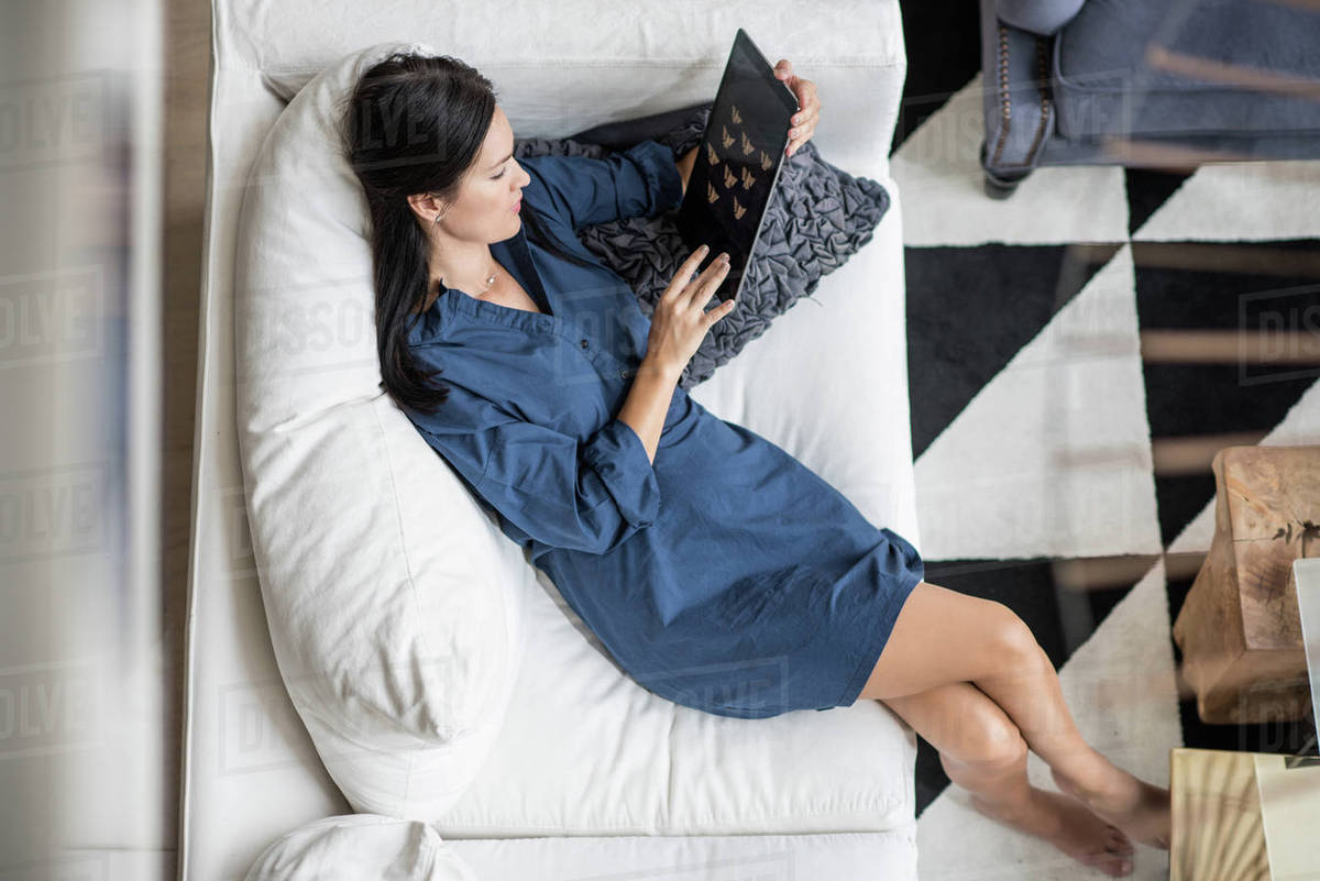 Overhead view of woman reclining on hotel room sofa using digital ...