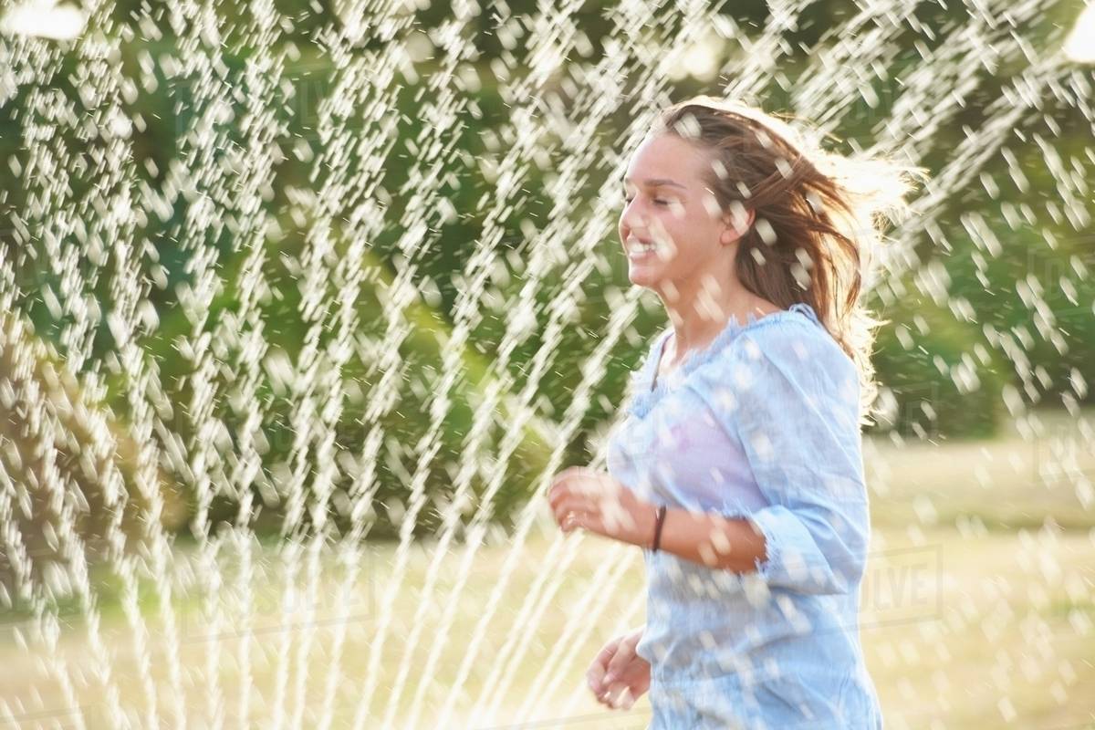 Woman running through sprinkler - Stock Photo - Dissolve