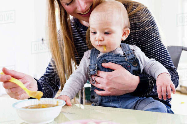 Woman feeding baby daughter at table - Royalty-free Stock Photo | Dissolve