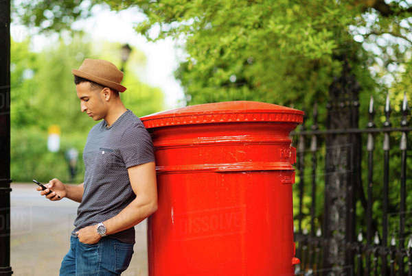 Man leaning against mailbox using smartphone - Stock Photo - Dissolve