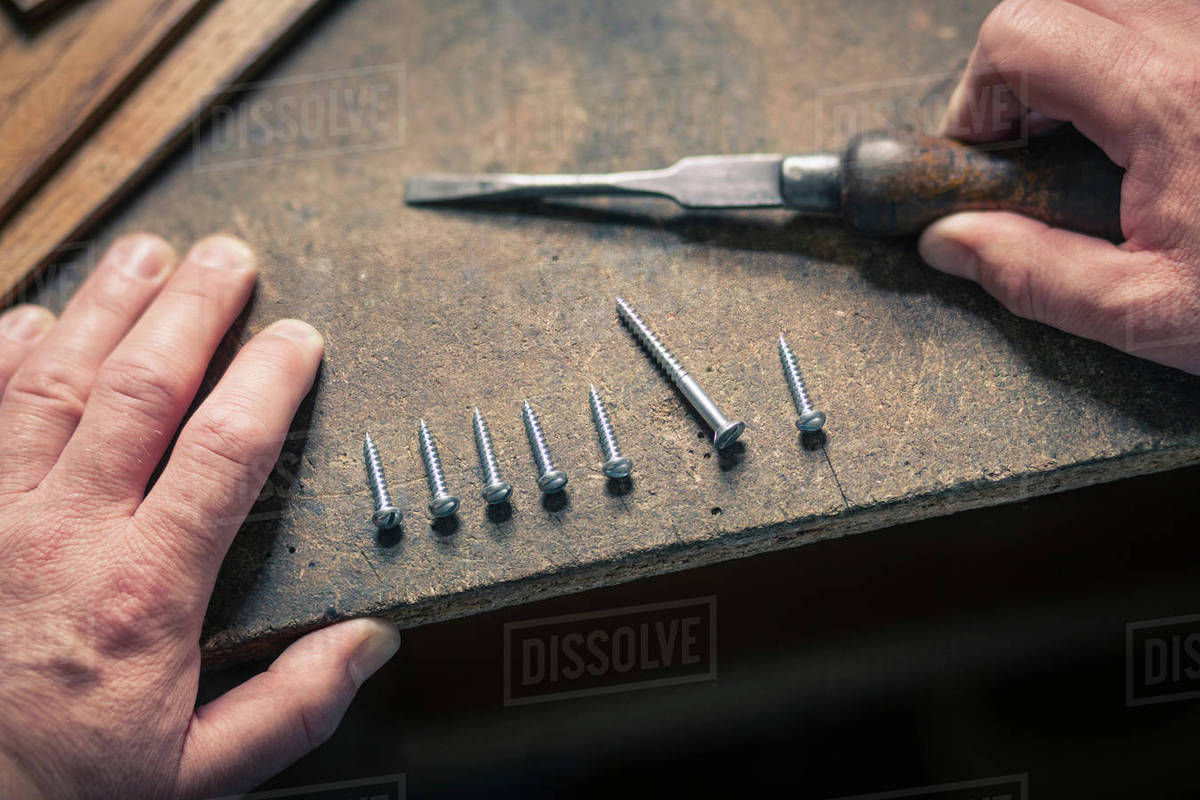 Hand holding chisel, screws in a row - Stock Photo - Dissolve