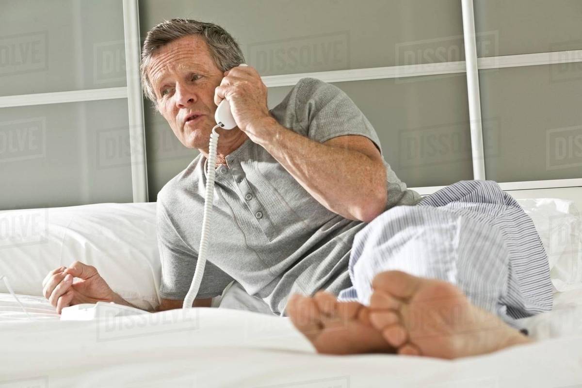 Senior man reclining on bed talking on landline telephone - Royalty ...
