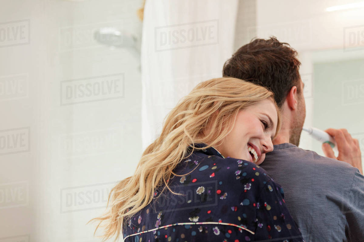 Couple in bathroom brushing teeth hugging - Stock Photo - Dissolve
