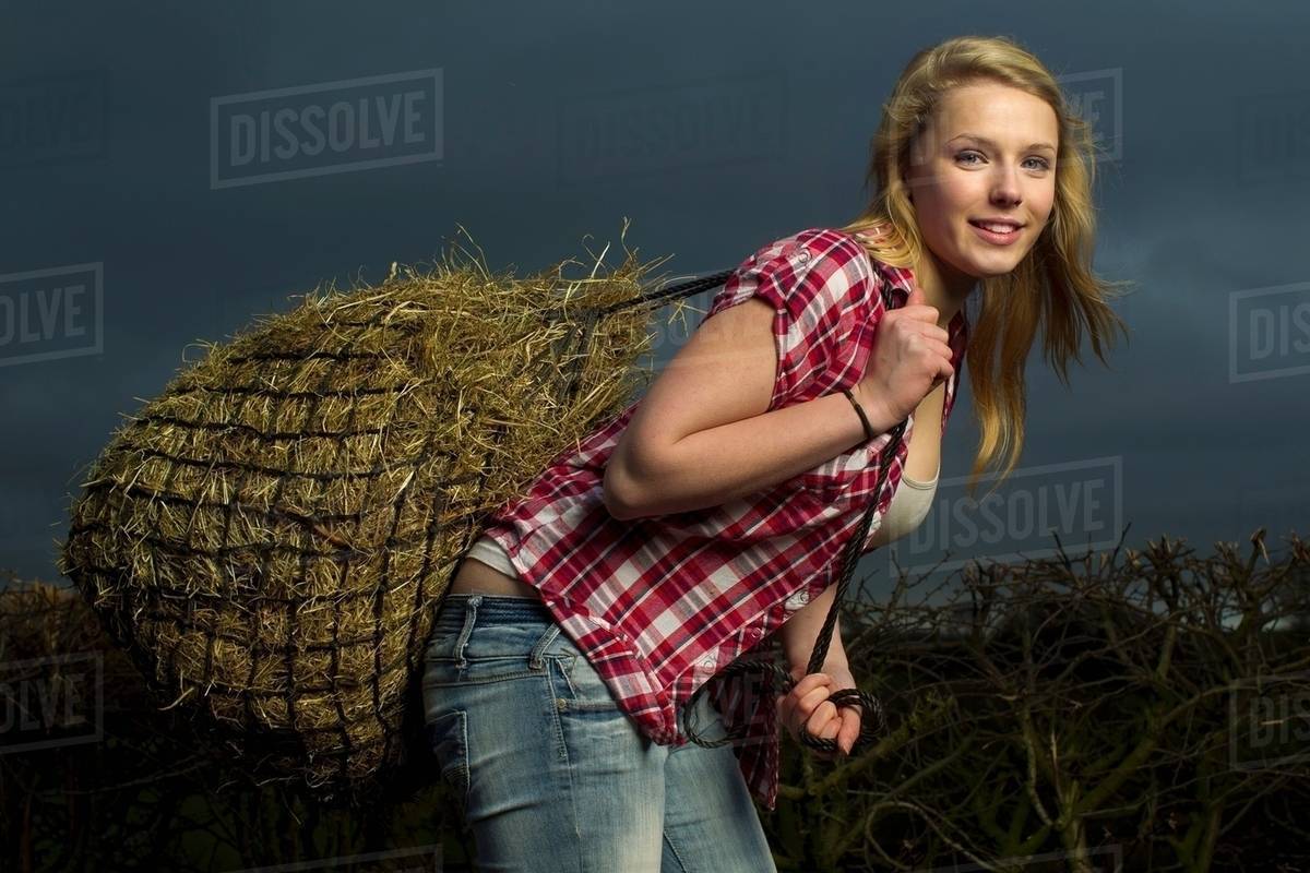Teenage girl carrying hay bales outdoors - Stock Photo - Dissolve