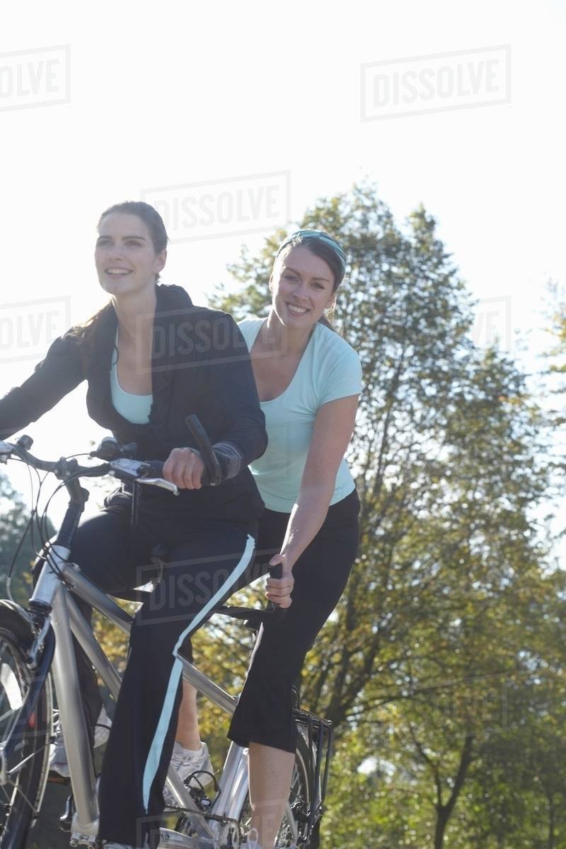 Smiling women riding tandem bicycle - Stock Photo - Dissolve