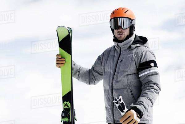 Man wearing helmet and ski goggles holding skis, portrait - Royalty ...