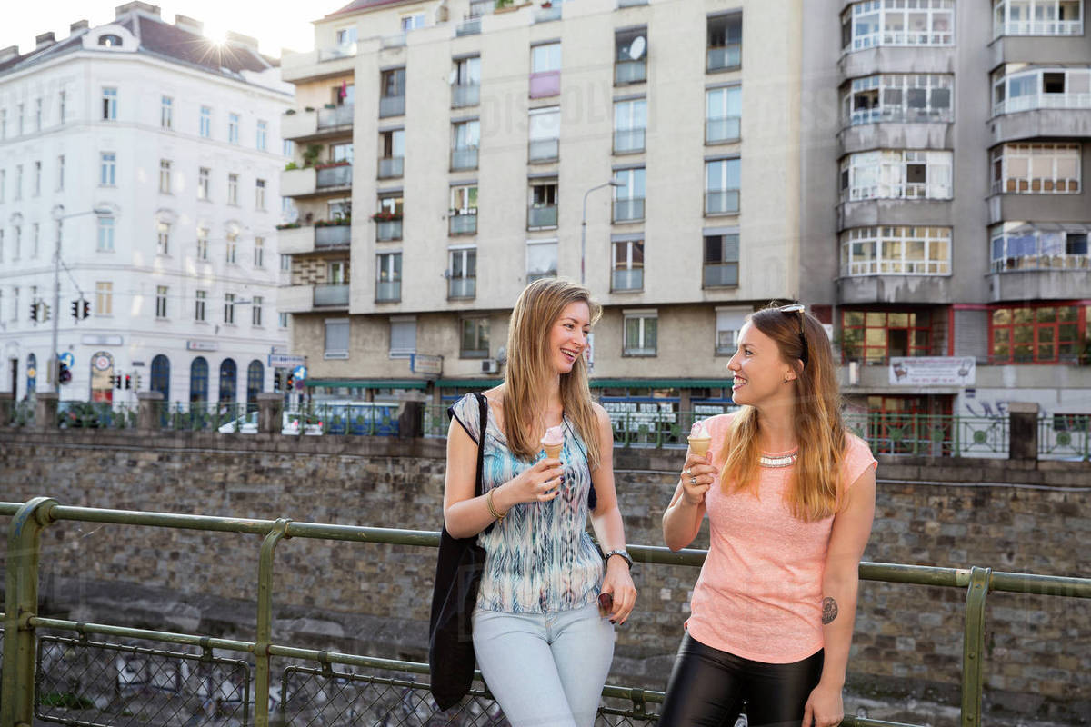 Two adult female friends eating ice cream cones and chatting in city ...