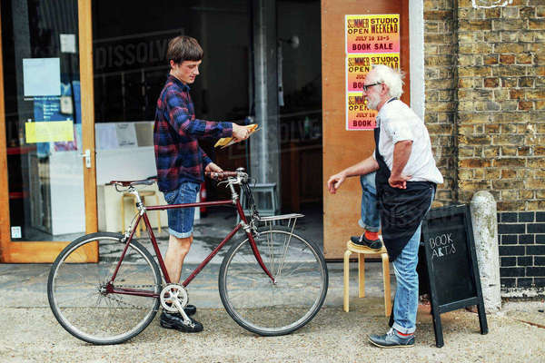 Young man with pushbike looking at post and standing with senior ...