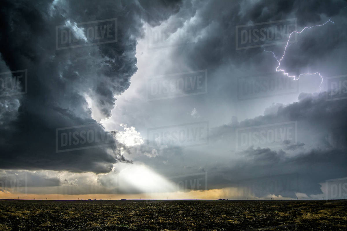 A supercell and tornado under the base of a storm, with beams of ...