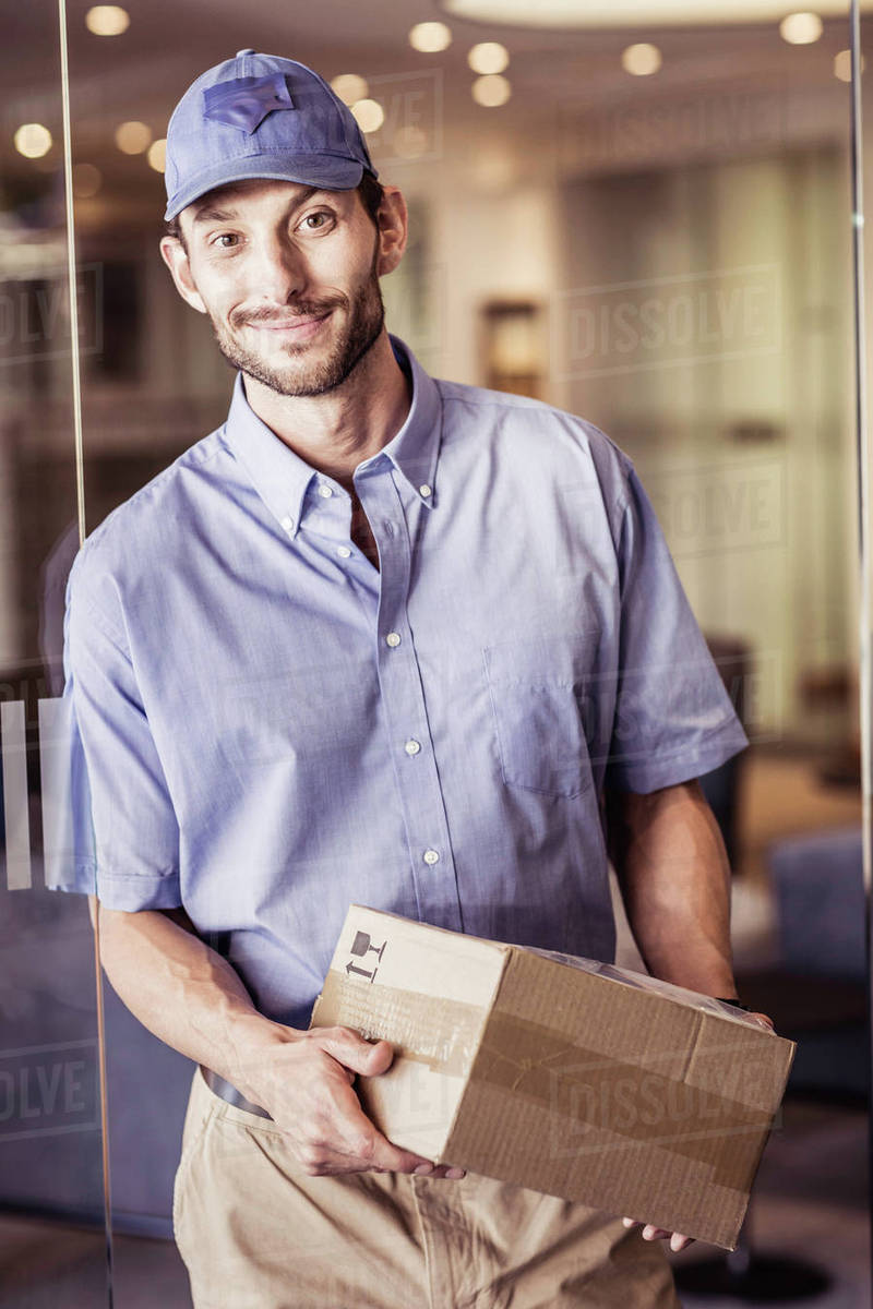 Portrait of delivery man carrying package in office - Stock Photo ...
