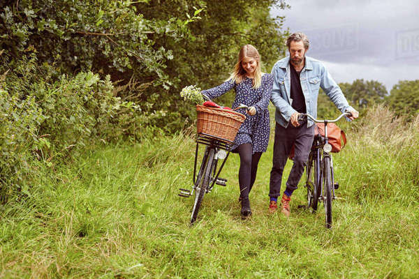 Couple pushing cycles along rural path - Stock Photo - Dissolve