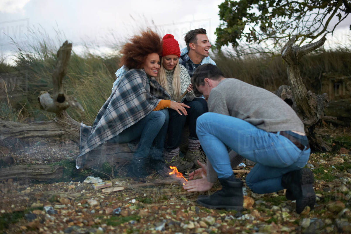 Four adult friends igniting campfire on windy beach - Stock Photo ...