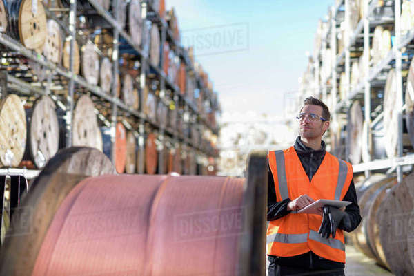 Worker inspecting cable reels with digital pad at cable storage ...