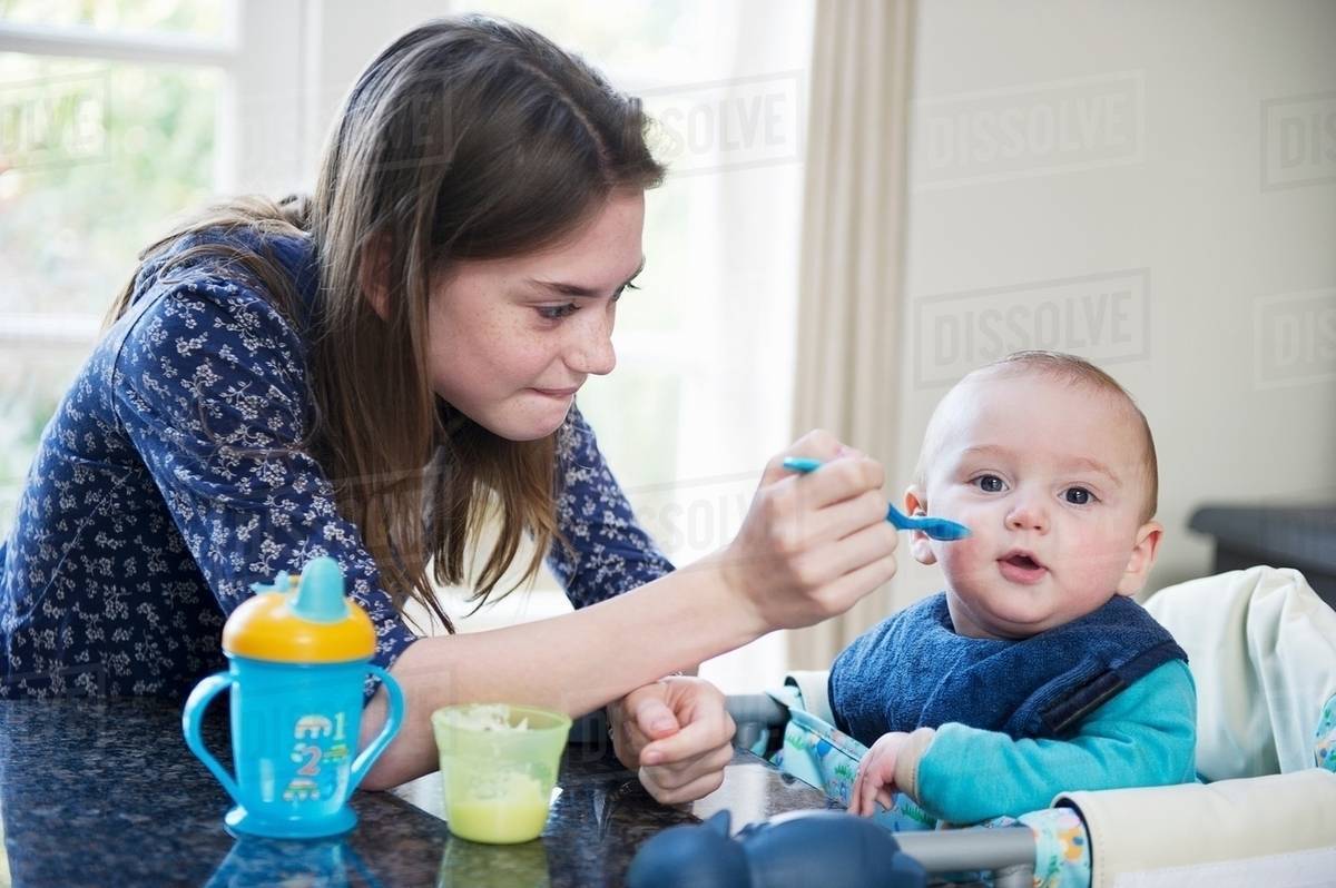 Girl feeding baby brother at table - Royalty-free Stock Photo | Dissolve