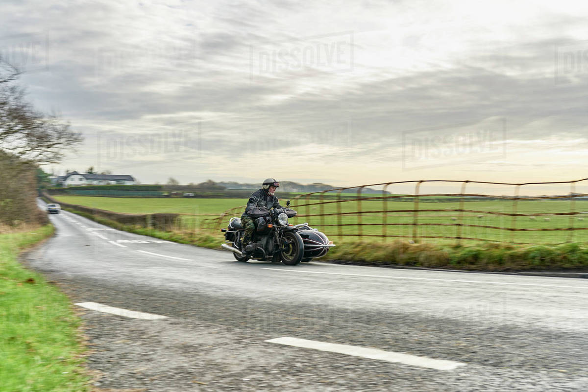 Senior man and grandson riding motorcycle and sidecar on rural road ...
