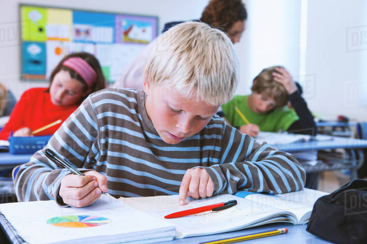 Boy sitting at desk, doing classwork - Stock Photo - Dissolve