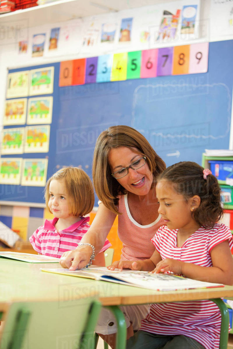 Preschool girls and teacher reading storybook in classroom - Royalty ...
