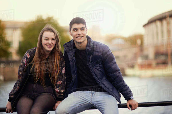 Portrait of two friends, sitting on railing by river, Bristol, UK ...