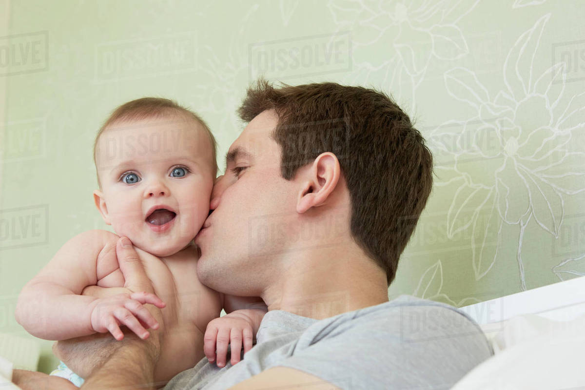 Mid adult man kissing baby daughter on cheek in bed - Royalty-free ...