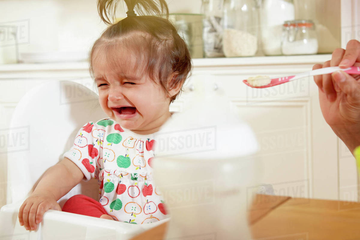 Baby girl crying while being fed breakfast by mother - Royalty-free ...