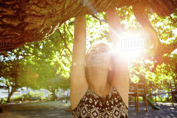 Girl hanging from tree branch, sun shining through trees - Royalty-free ...