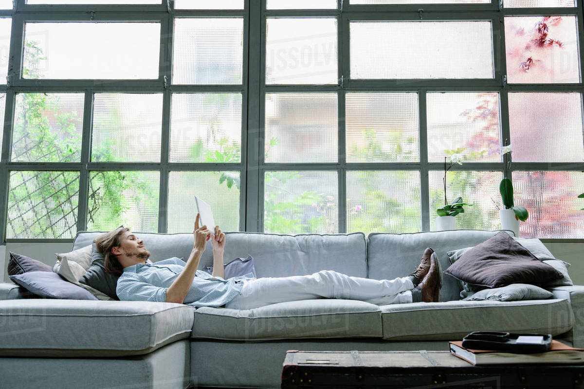 Man lying on sofa using digital tablet - Stock Photo - Dissolve