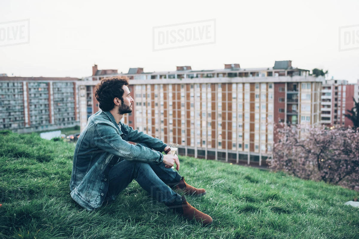 Young man sitting on rooftop garden, looking at view - Royalty-free ...