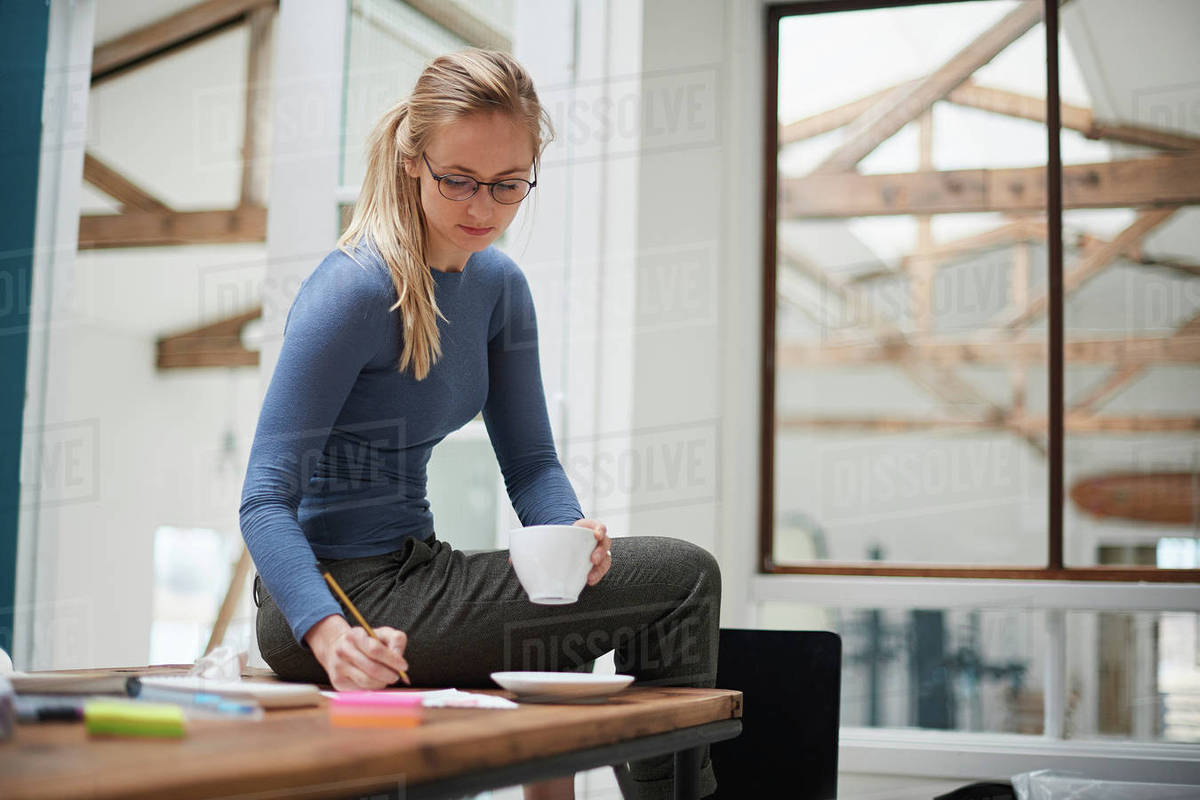 Female designer writing notes while sitting on design studio desk ...