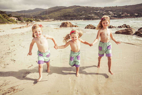 Three young sisters holding hands, running along beach, smiling - Stock ...