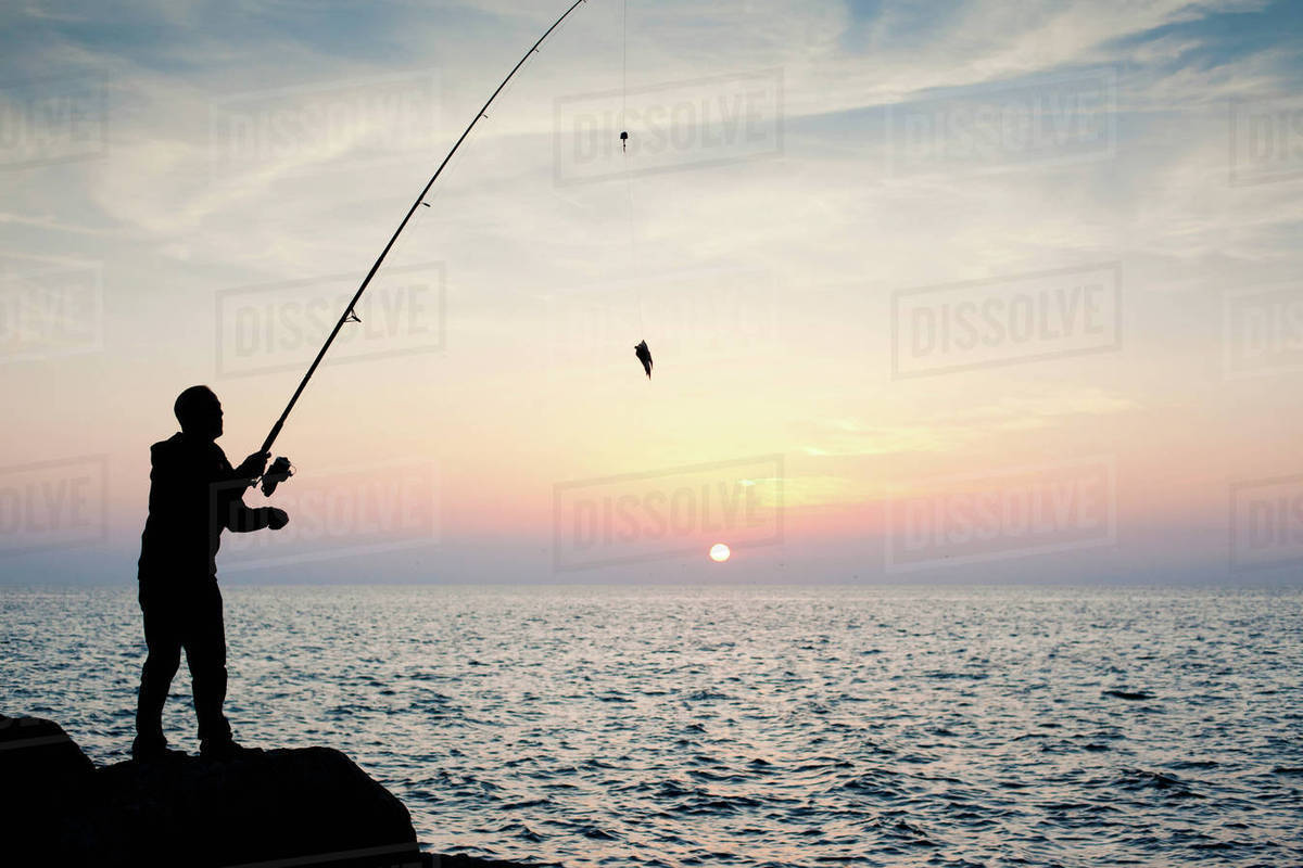 Silhouette of man fishing at sunset - Royalty-free Stock Photo | Dissolve