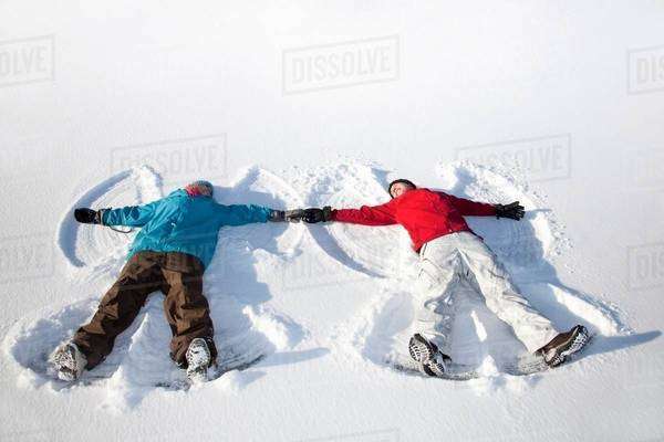 Couple making snow angels outdoors - Stock Photo - Dissolve
