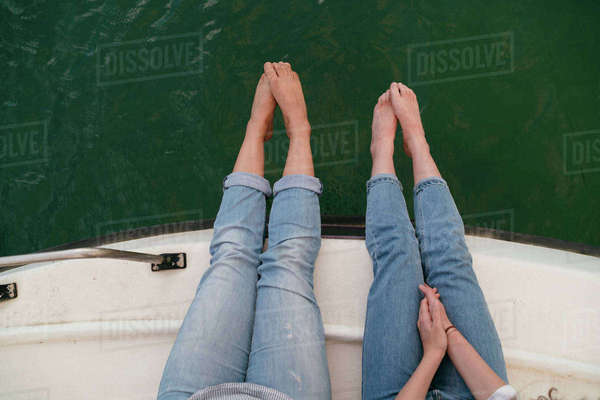 Two women, relaxing on boat, feet over edge of boat, barefoot, overhead ...