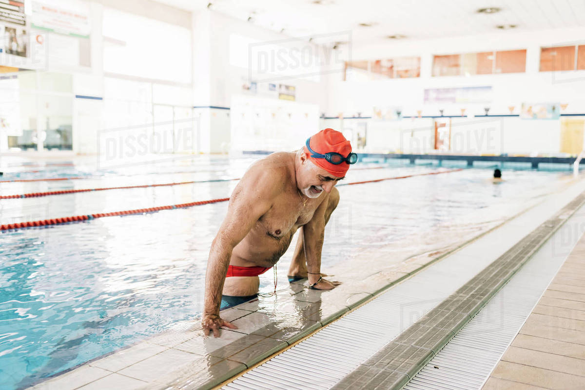 Senior man climbing up side of swimming pool - Stock Photo - Dissolve