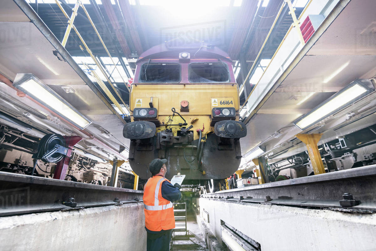 Engineer inspecting locomotive in train works - Stock Photo - Dissolve