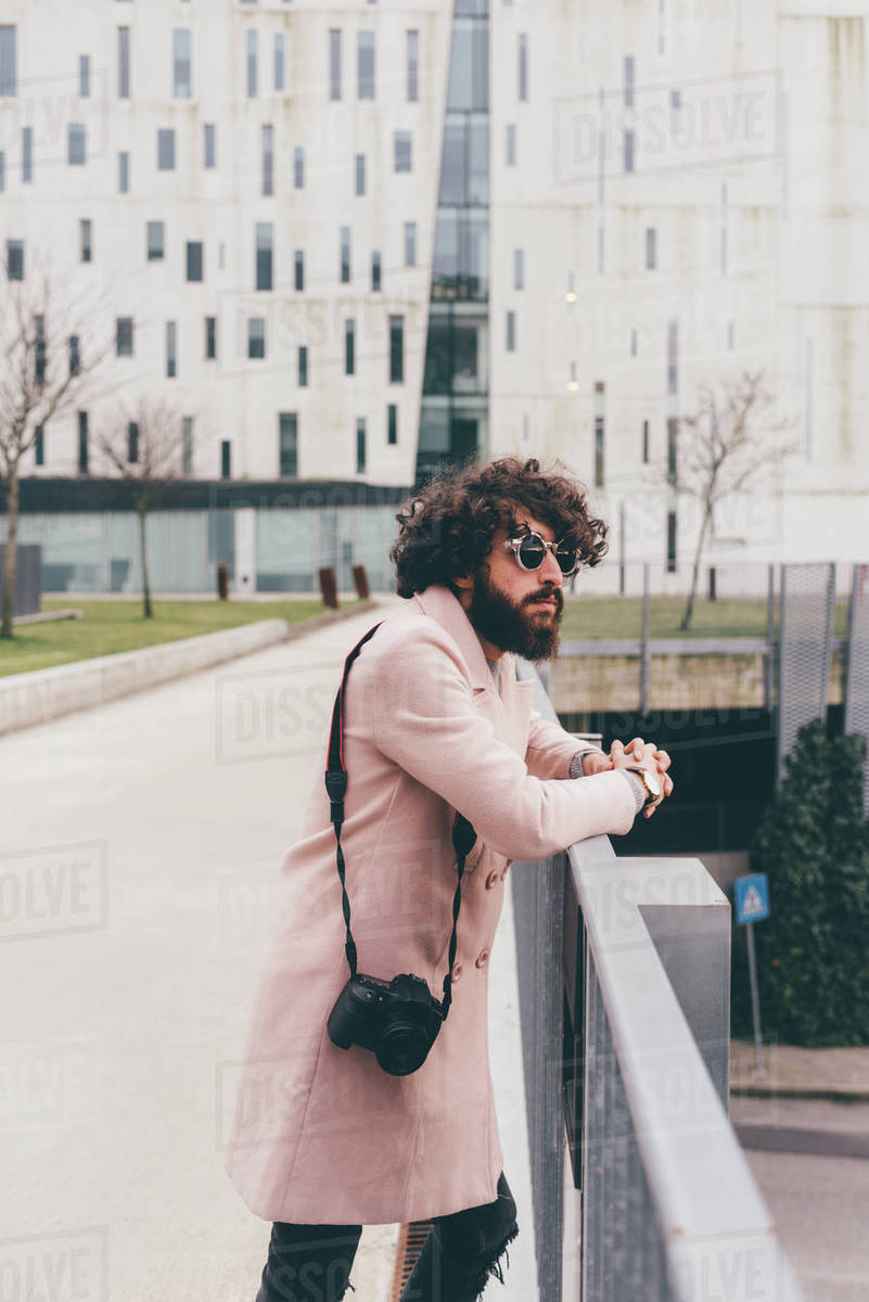 Young man standing on bridge, looking at view, camera over shoulder ...