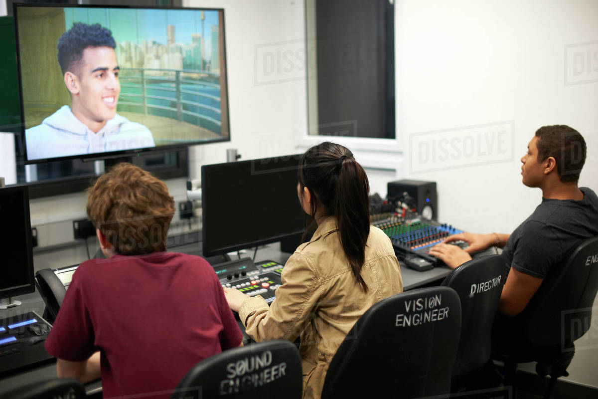 Young male and female college students at mixing desk watching TV ...