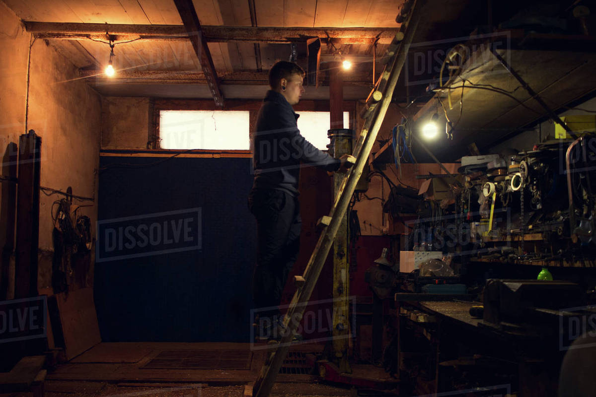 Mechanic on ladder looking at shelves in workshop - Royalty-free Stock Photo | Dissolve